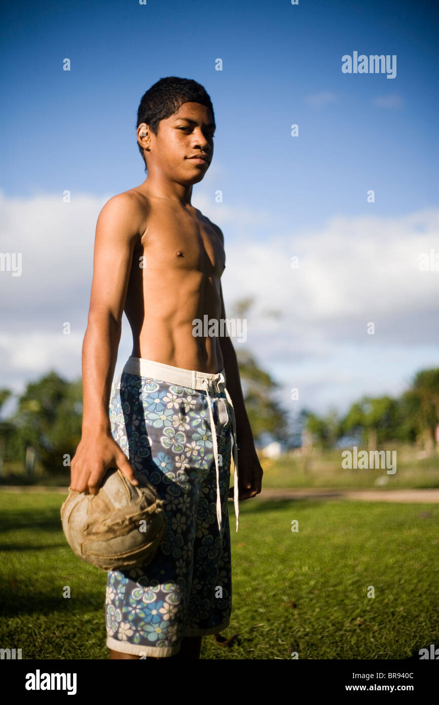 A portrait of a young man at sunset holding a beaten up soccer ball ...