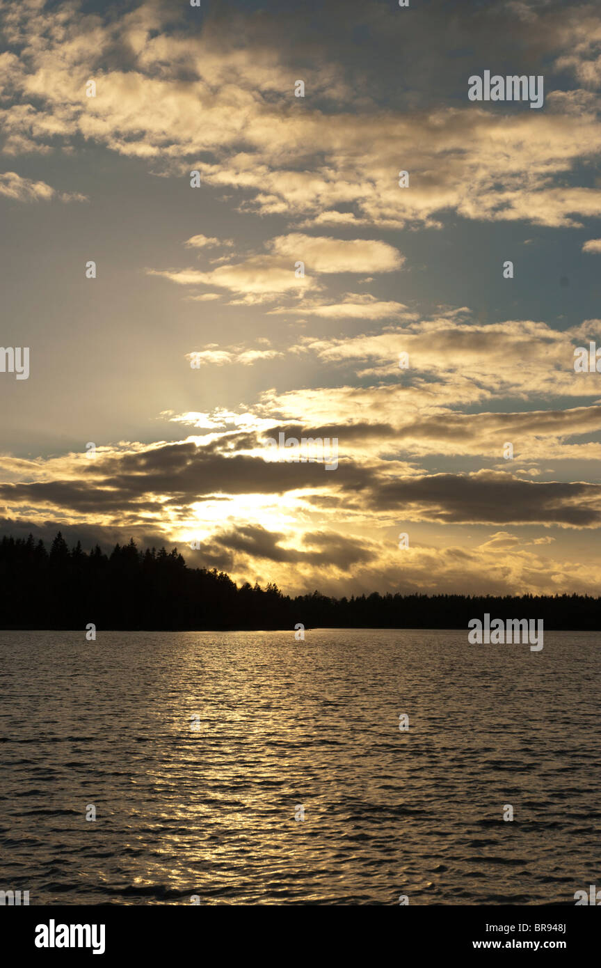 sun breaking through clouds reflecting off lake in Sweden Stock Photo ...