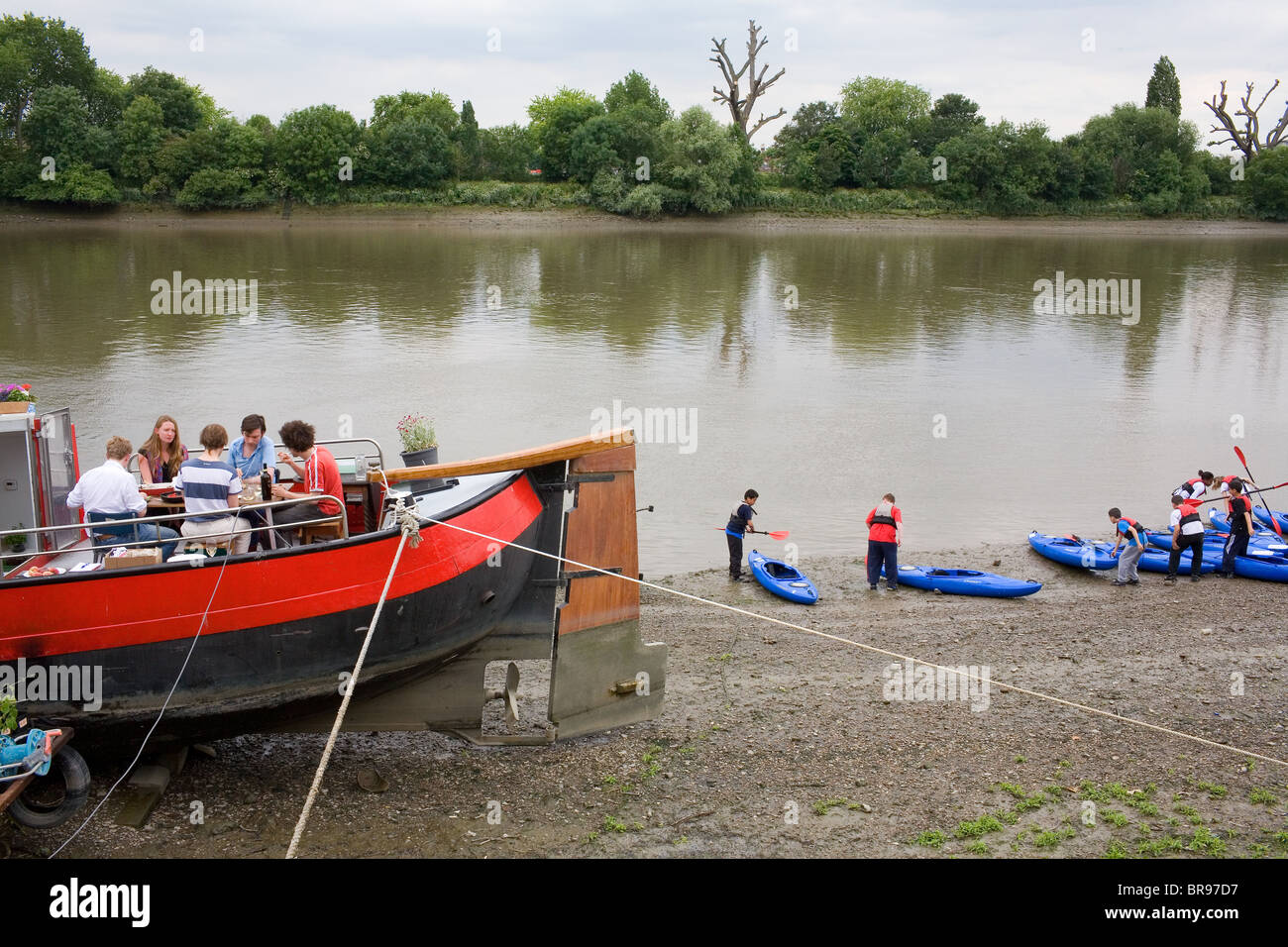 Friends eat lunch on a canal bot moored next to Hammersmith Bridge on ...