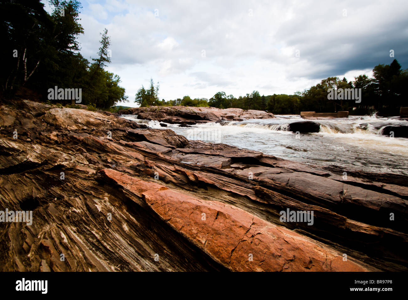 A river flows by layered rocks Stock Photo - Alamy