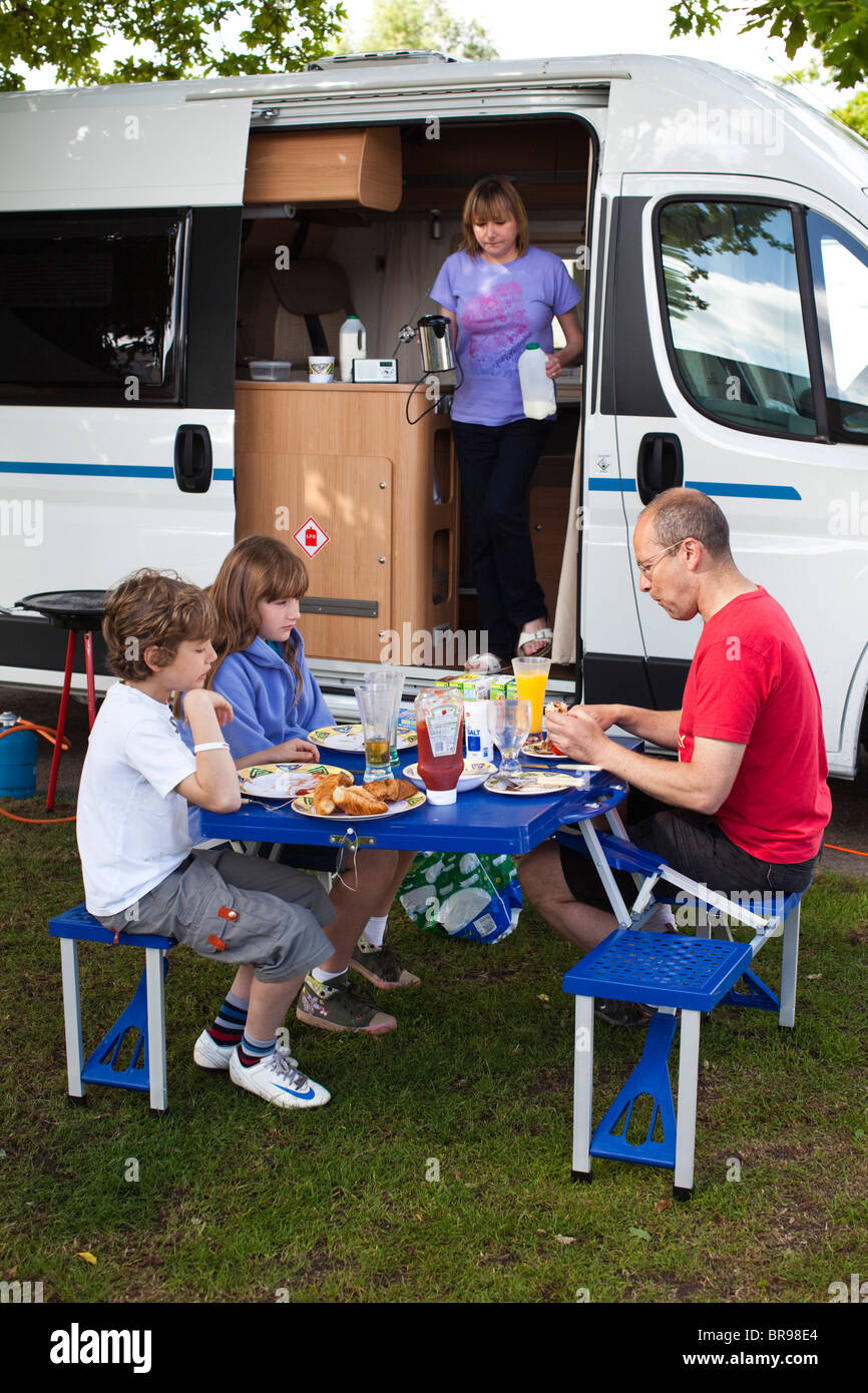 A family eating breakfast together outside their motorhome in a caravan ...