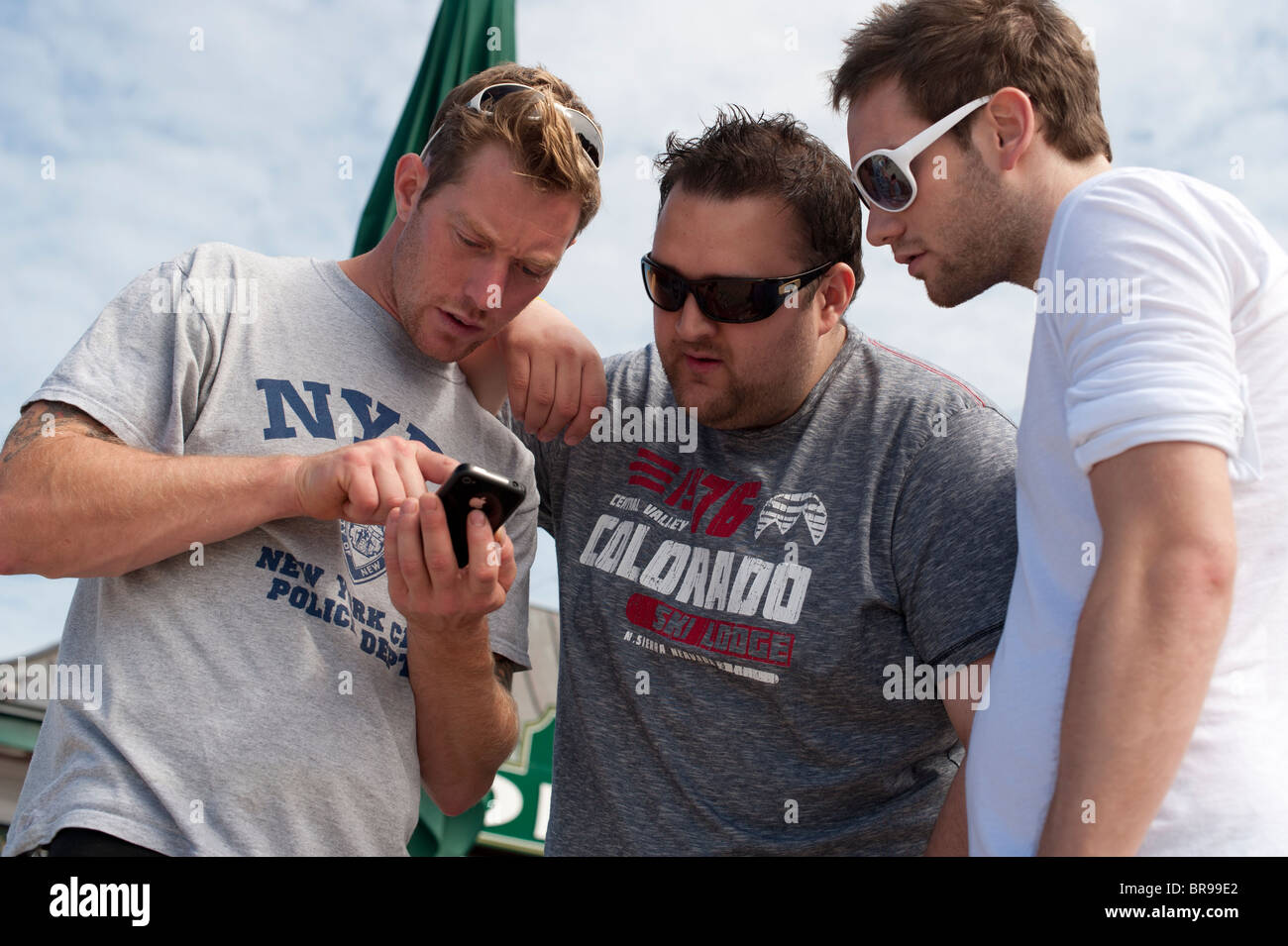 Three young men in their 20s looking at an app or checking emails and ...
