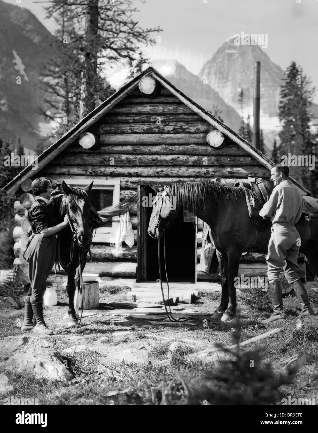 1920s 1930s COUPLE IN FRONT OF LOG CABIN STANDING BY HORSES WITH ...