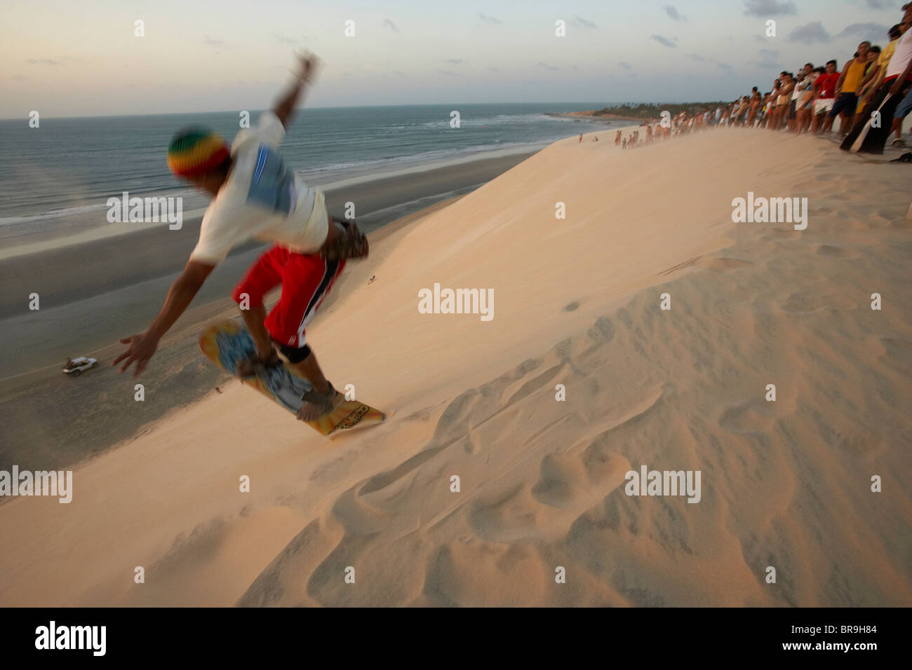 Brazilian man sandboarding jumps off dune while a crowd watches ...