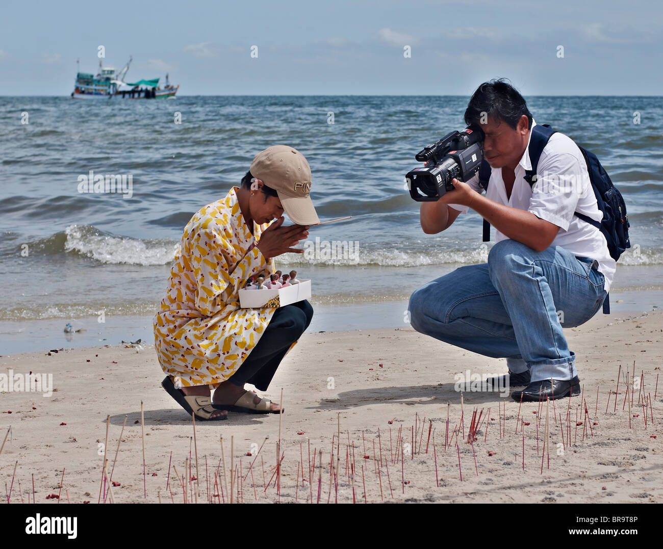 News media cameraman filming a Thai woman on a beach praying. Thailand ...
