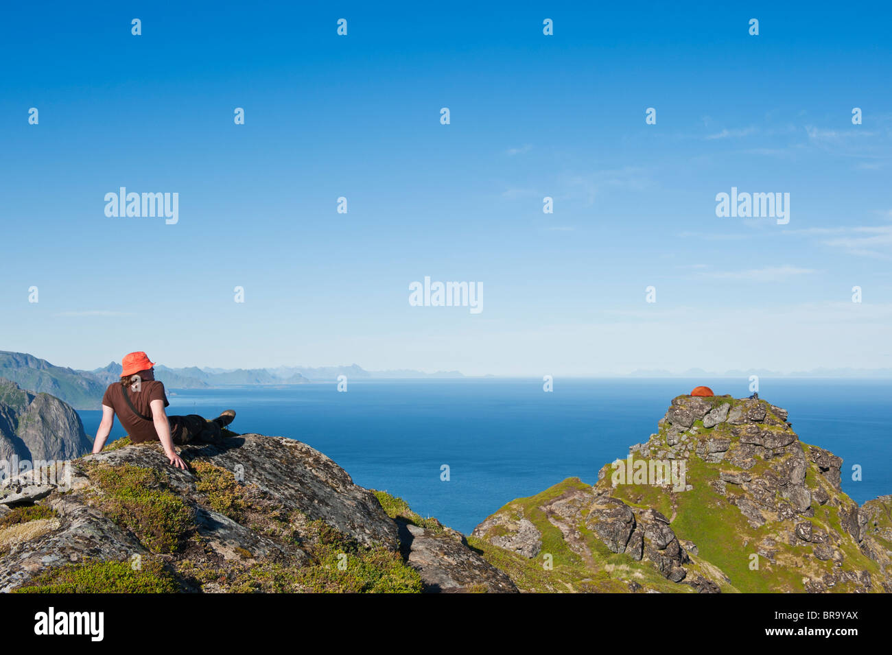 Hiker sits on mountain peak near Reinebringen, Moskenesoy, Lofoten ...