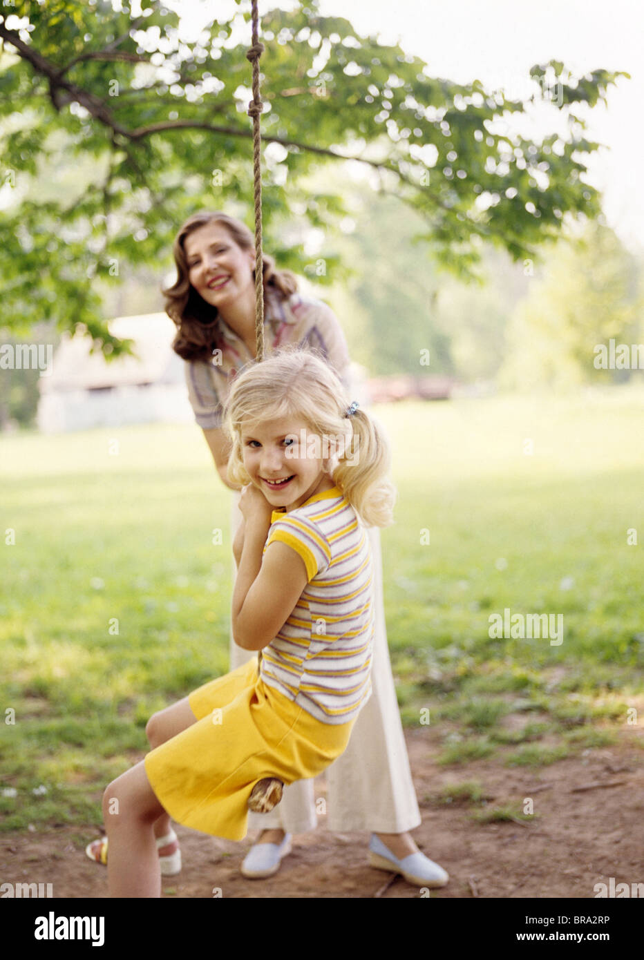 1970 1970s RETRO SMILING WOMAN MOTHER WITH GIRL DAUGHTER SWINGING PLAYING ON ROPE SWING ON TREE ...