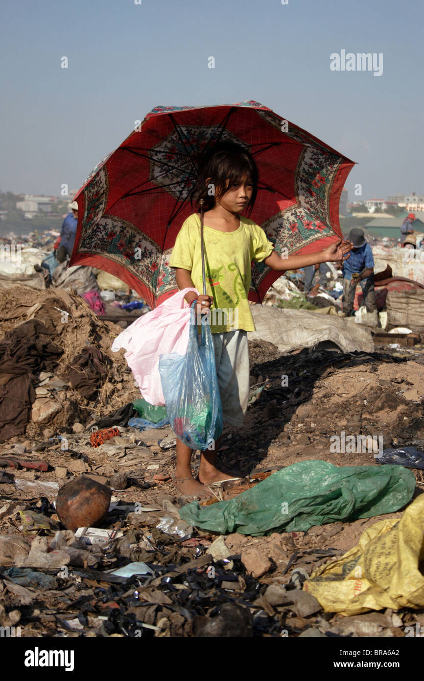 A young child laborer girl is carrying an umbrella to shade herself at ...