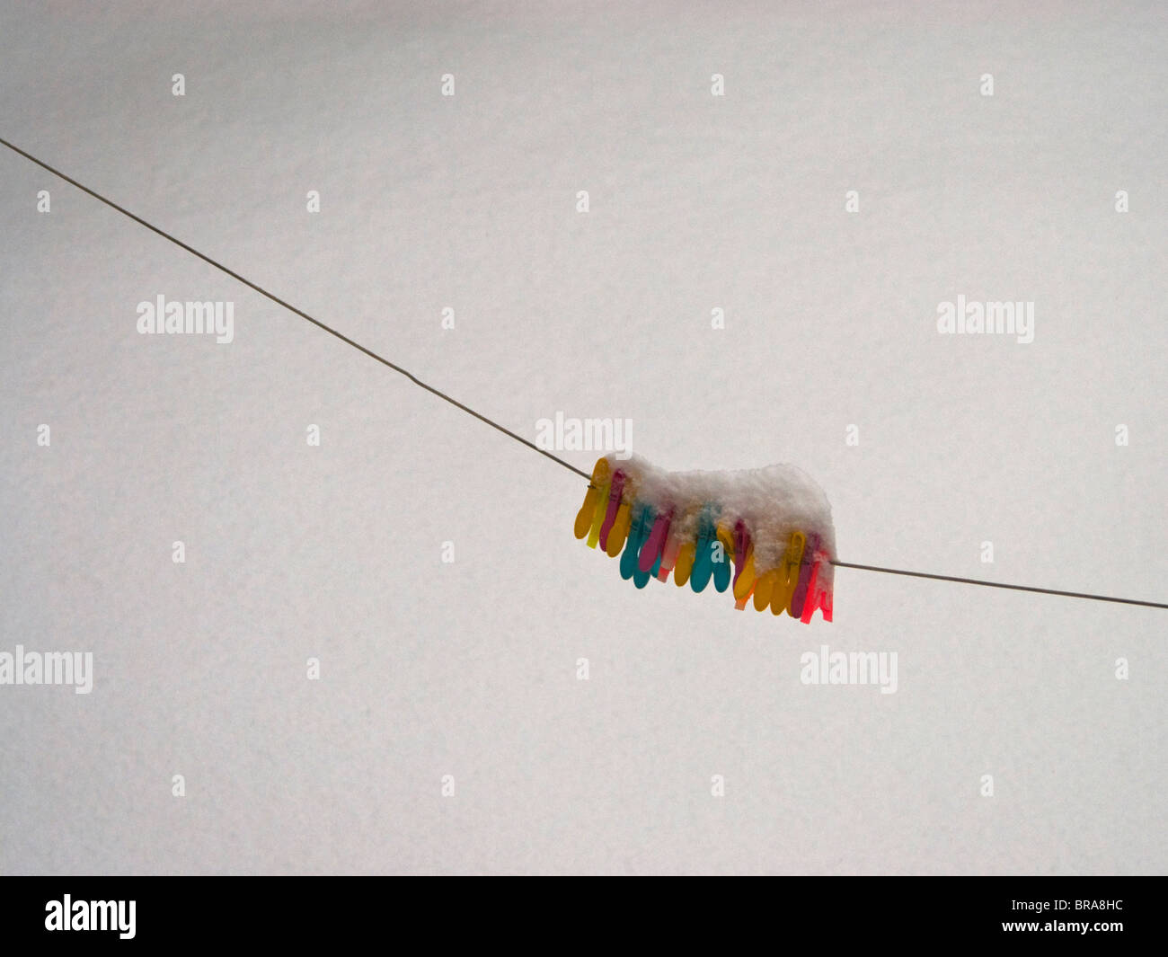 Colourful clothes pegs on a washing line in winter, topped with snow ...