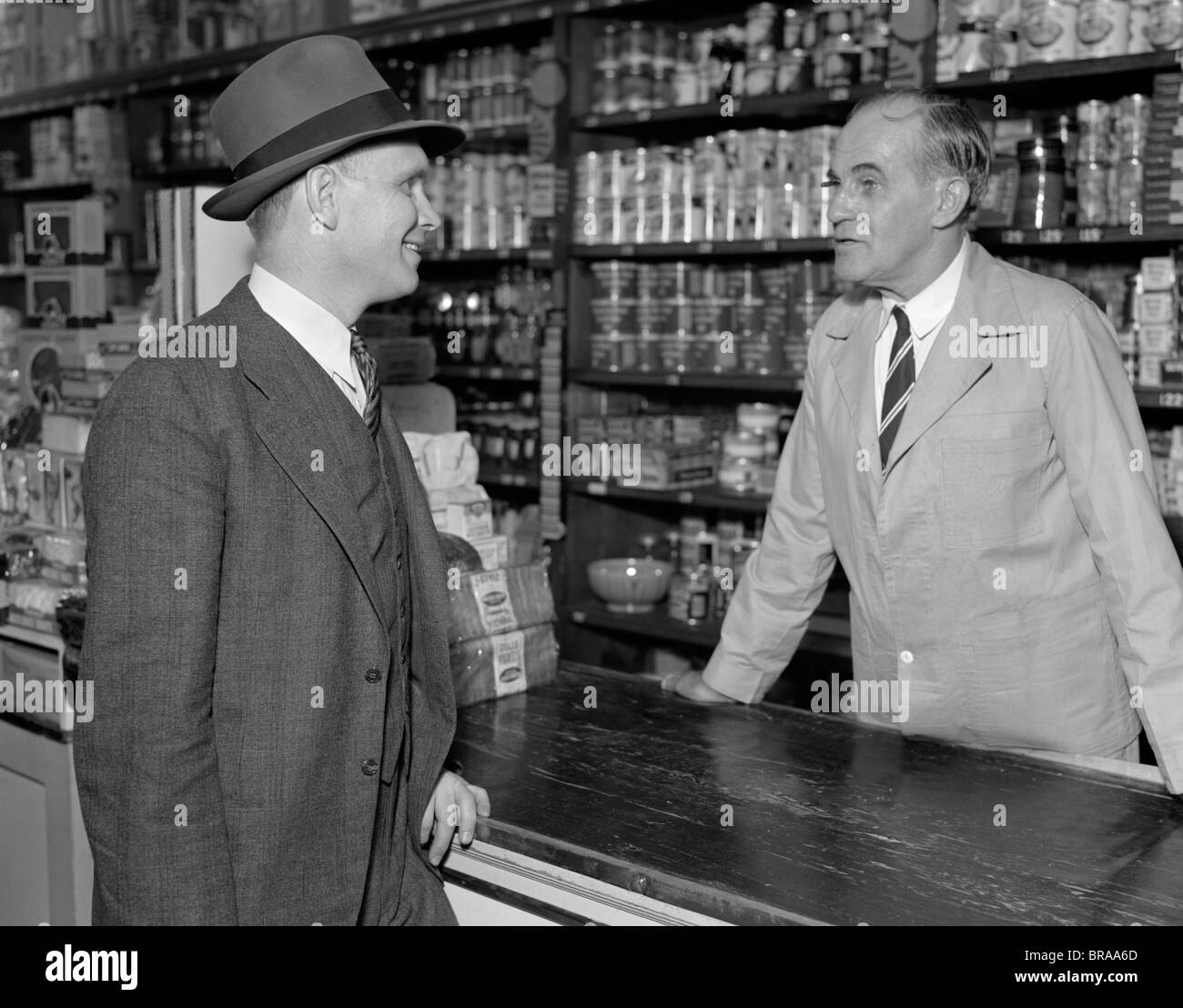 1930s TWO MEN CLERK AND CUSTOMER TALKING OVER COUNTER IN RETAIL GENERAL ...