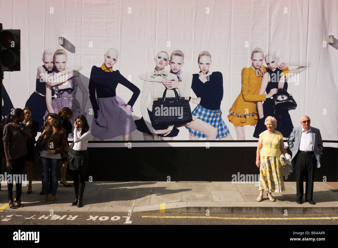 Young women on a shop hoarding with pedestrians and an elderly couple ...