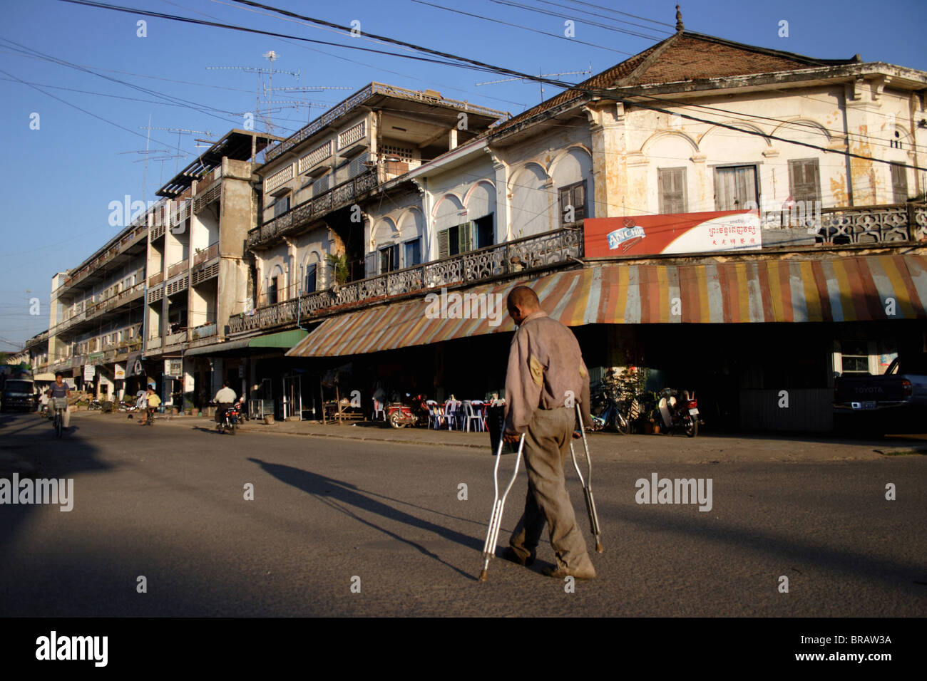 A man with crutches walks down the middle of a main street casting a ...