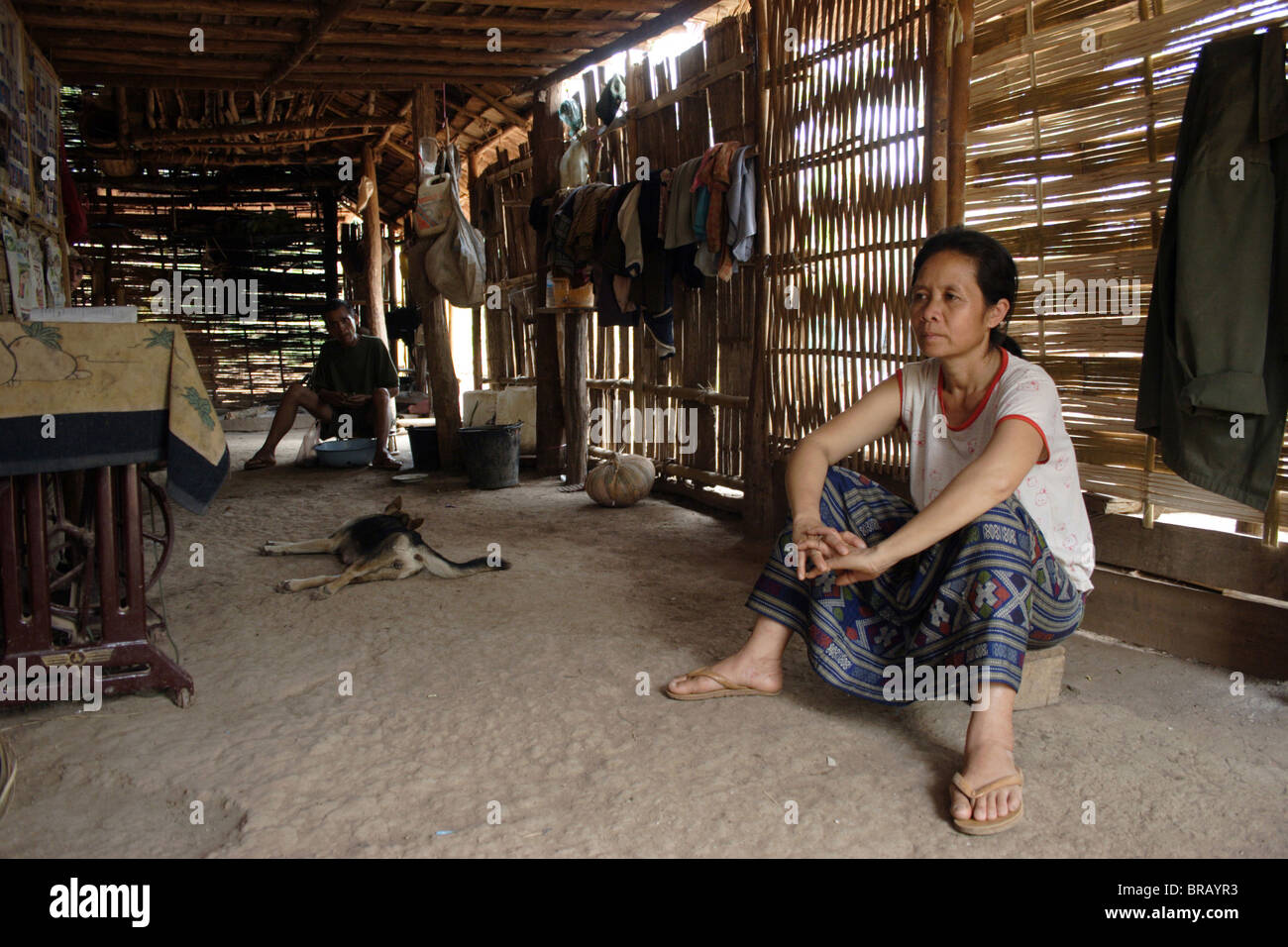 A subsistence farmer who is living in poverty sits on a small stool in ...