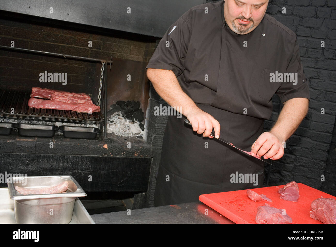 A chef in black uniform cutting raw meat Stock Photo - Alamy