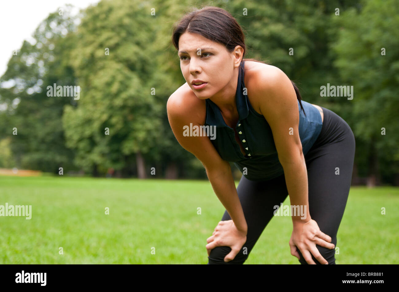 Young woman having break after jogging in park - leaning agains knees ...