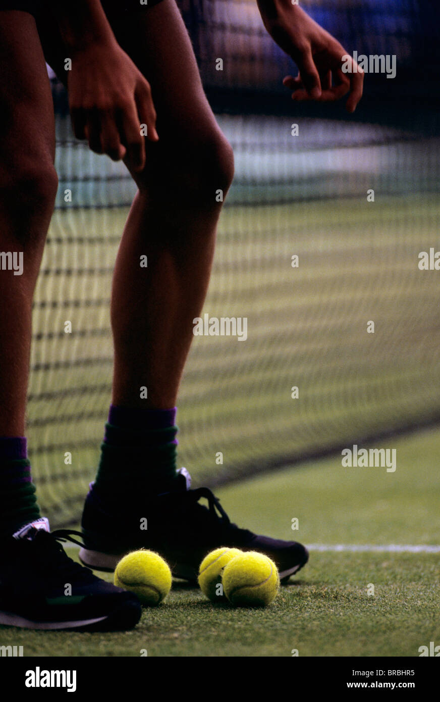 Yellow tennis balls on ground between legs of ball boy on grass court ...