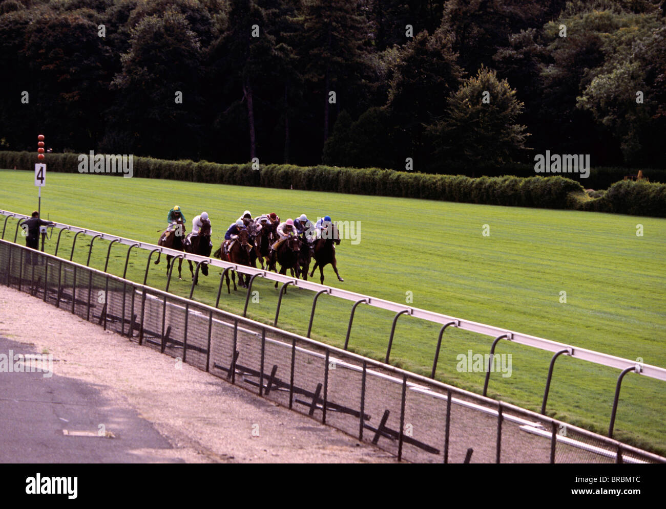 Group of horses and jockeys past the four furlong marker on race course ...