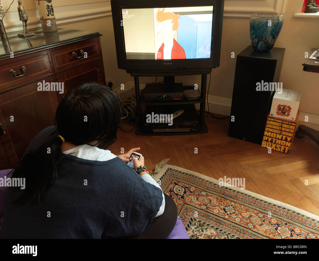 A Teenage Girl Texting on a Mobile Phone While Watching Television ...