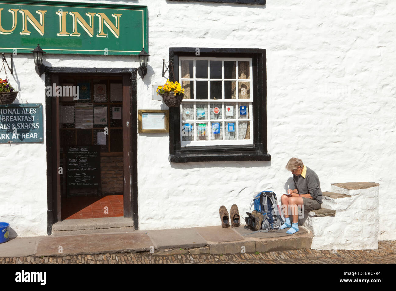 A woman hiker writing postcards on the old mounting block outside the ...