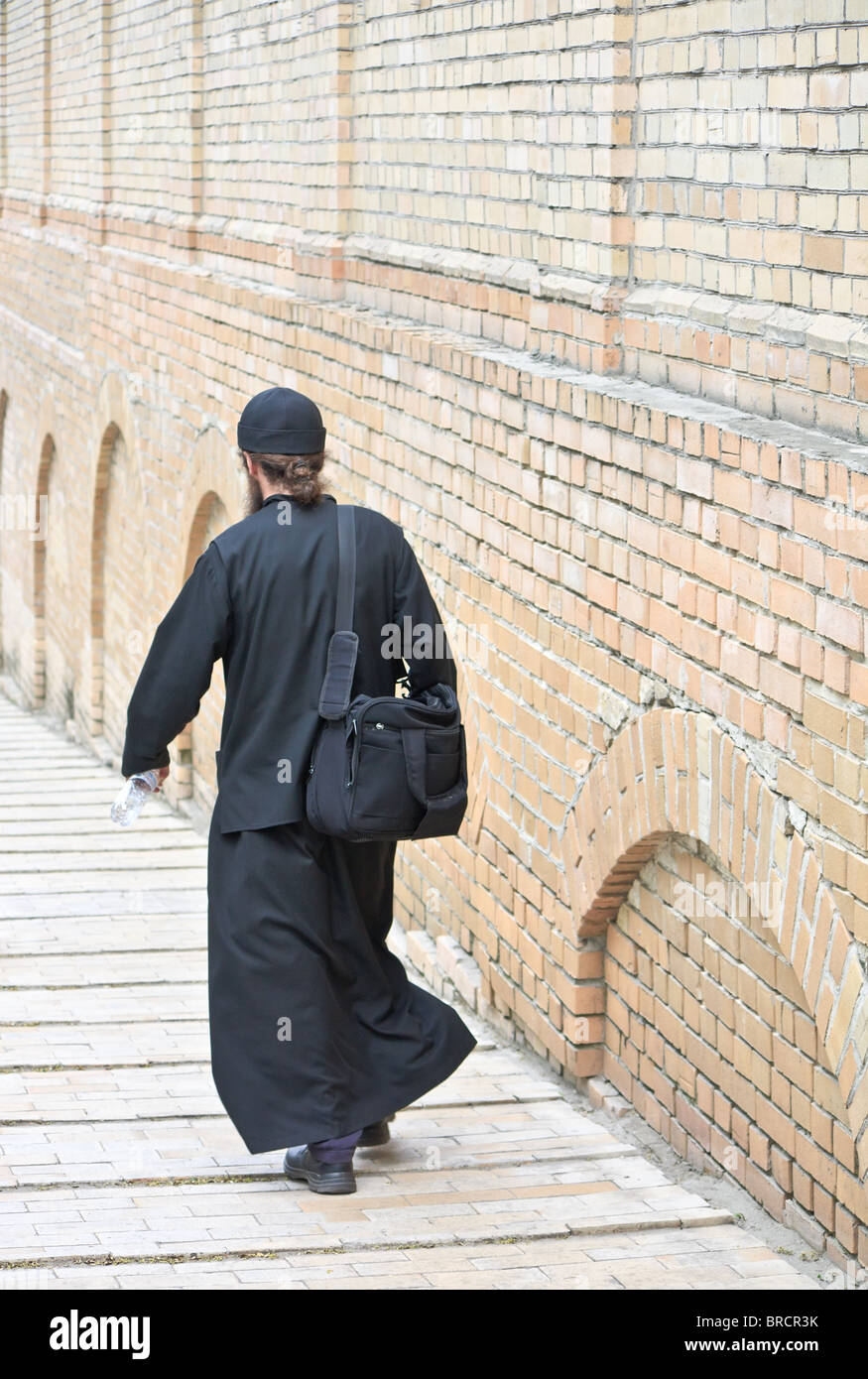Young ortodox monk in black cassock against the brick monastery wall ...