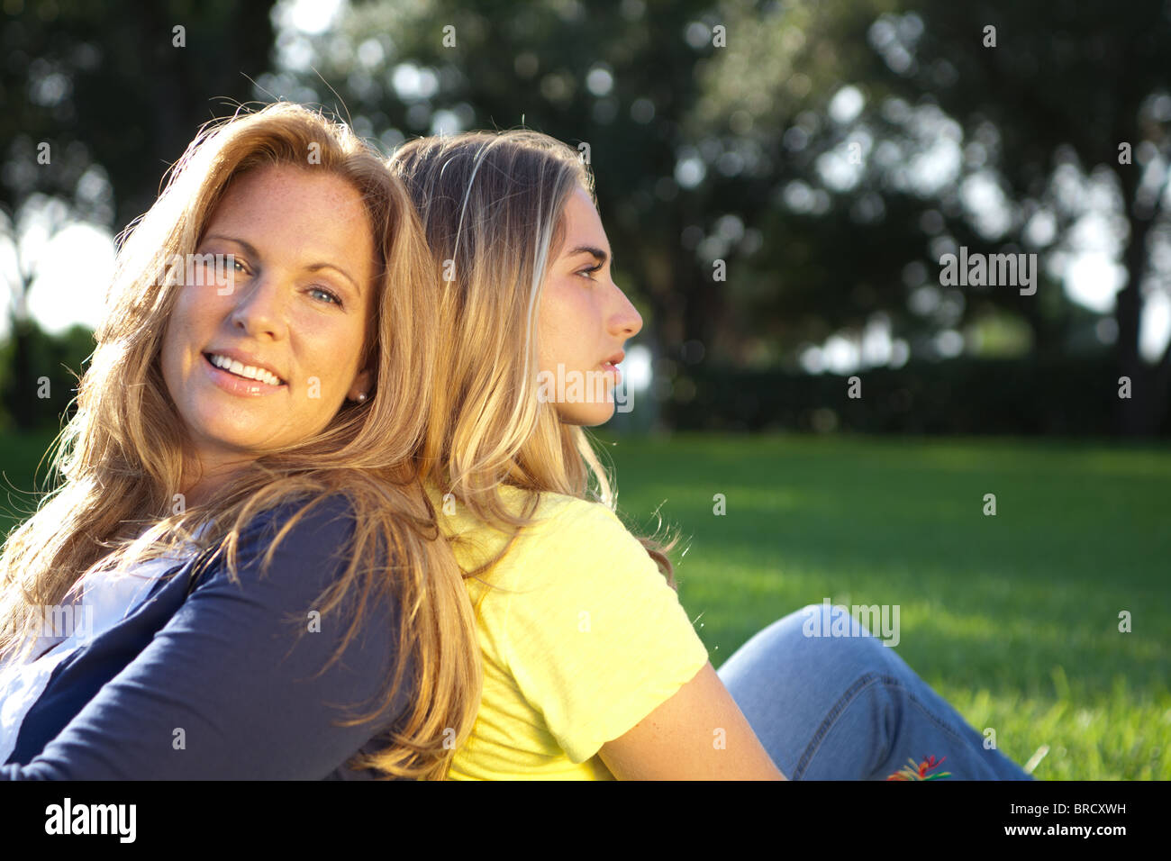 Mother And Daughter Sit At The Park Resting Their Backs To Each Other 2292