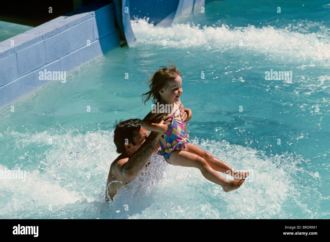 Father And Daughter Enjoying A Giant Water Slide Splashing Into Water