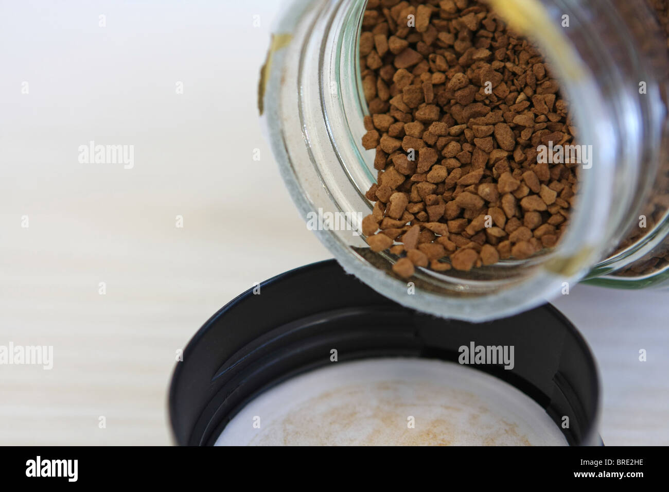 Coffee granules in a jar, which is on its side and resting on its lid ...
