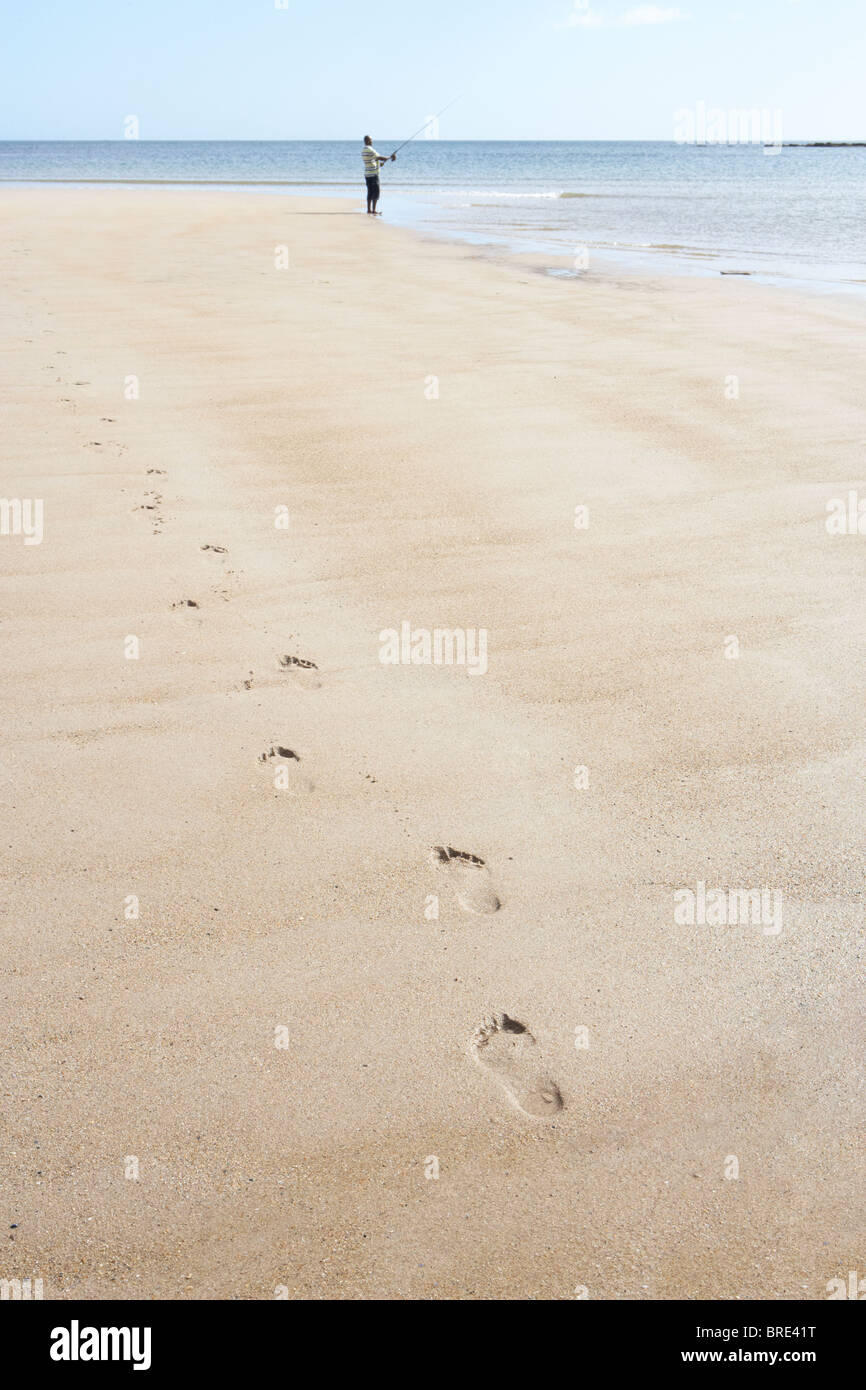 Man Walking Along Shore Of Beach Carrying Fishing Rod Stock Photo - Alamy