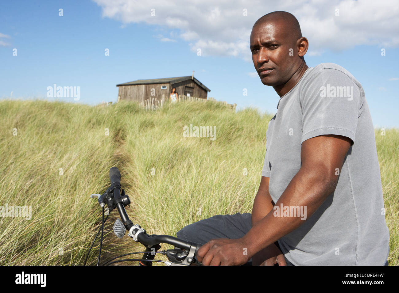 Young Man Riding Mountain Bike By Dunes With Old Beach Hut In Distance ...