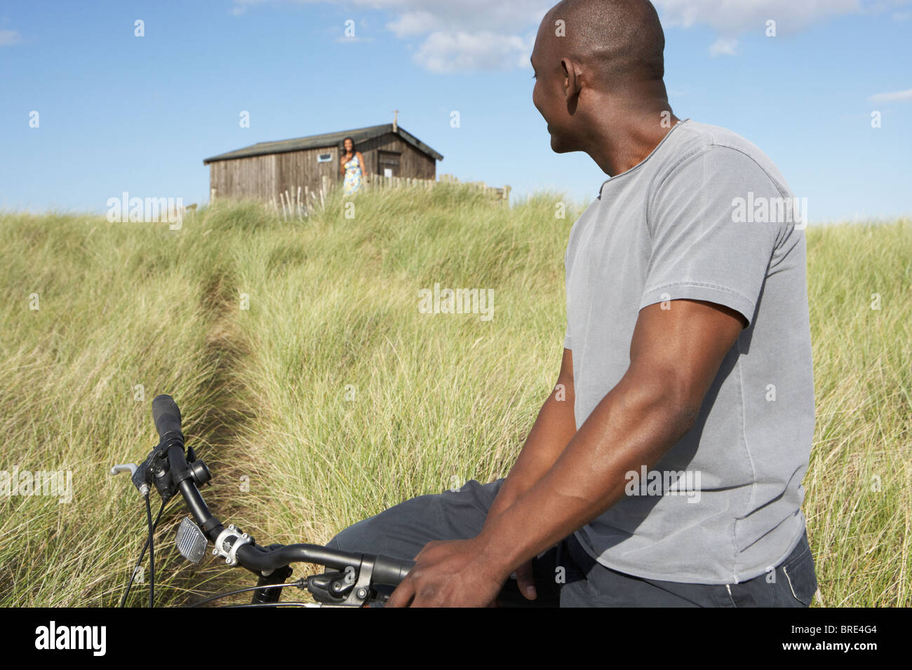 Young Man Riding Mountain Bike By Dunes With Old Beach Hut In Distance ...