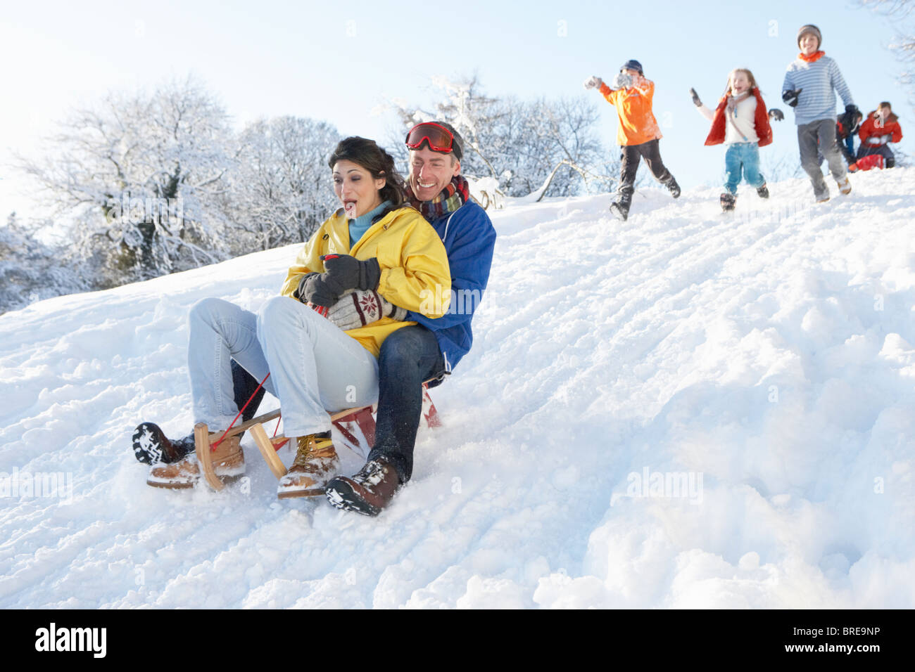 Young Couple Sledging Down Hill With Family Watching Stock Photo - Alamy