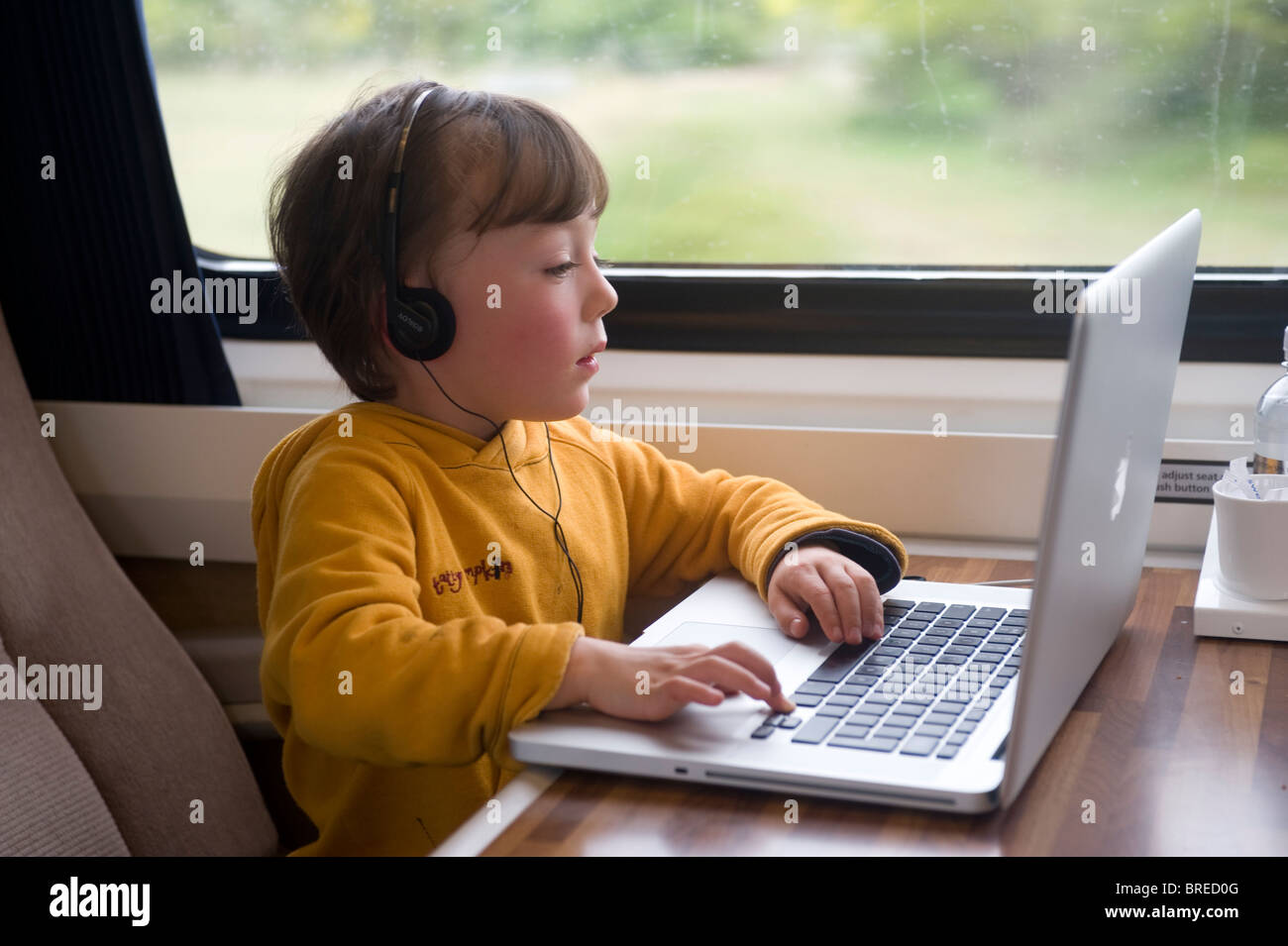 young boy playing games on an apple mac computer on a train journey ...