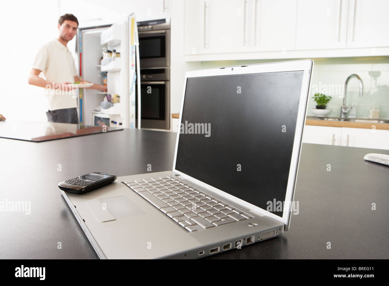 Young Man Fixing Snack In Kitchen With Laptop In Modern Kitchen Stock ...