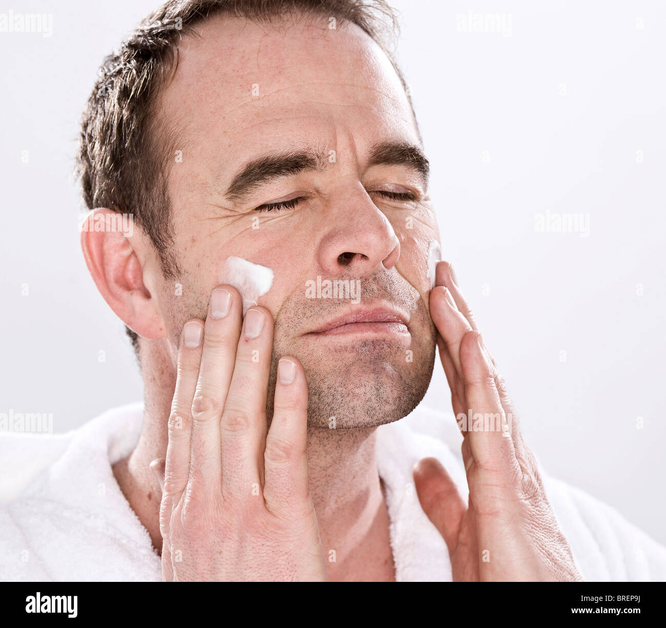 Man wearing a bathrobe, relaxed, putting lotion on his face Stock Photo ...