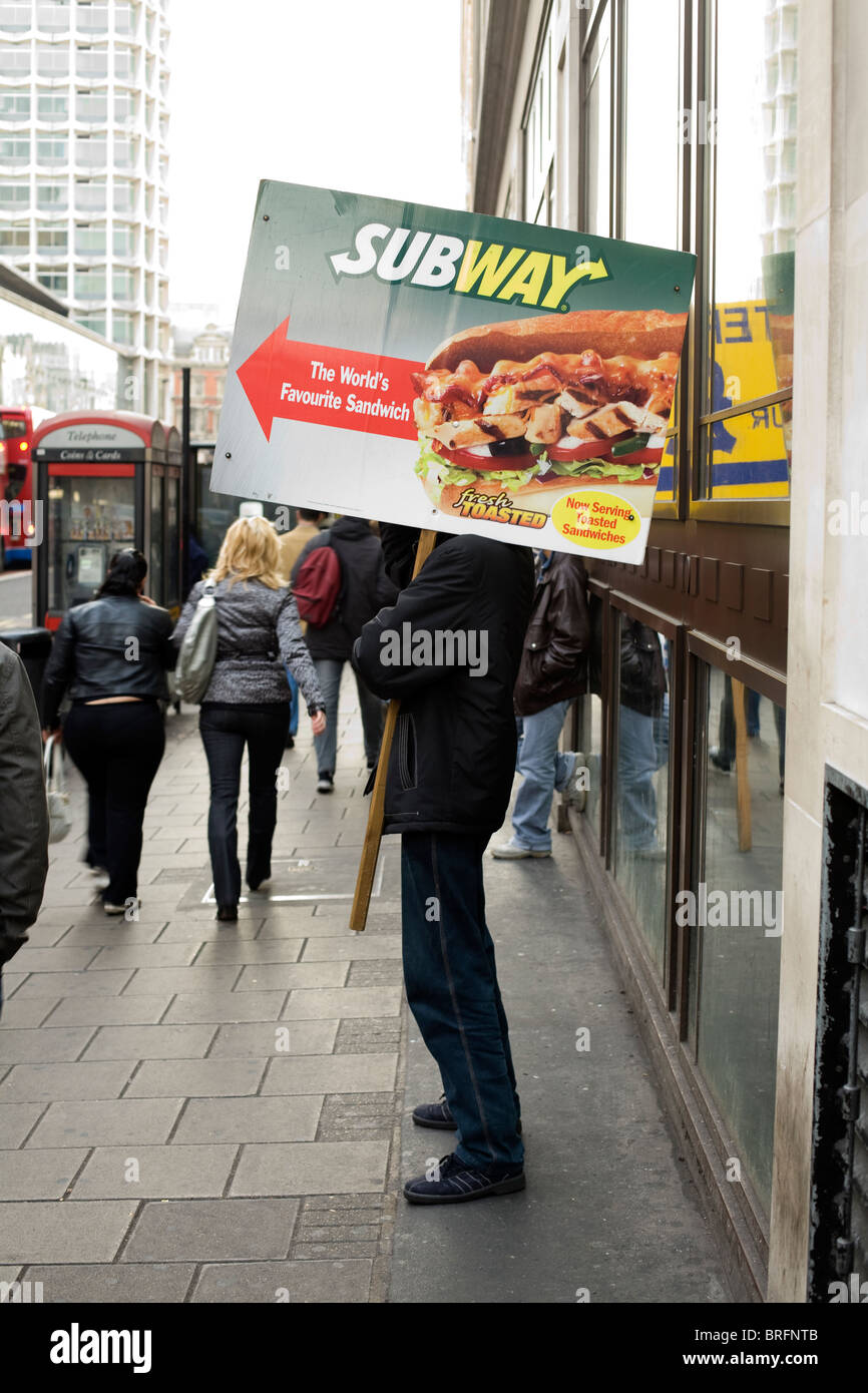 A man carrying an advertisement sandwich board in an urban central ...