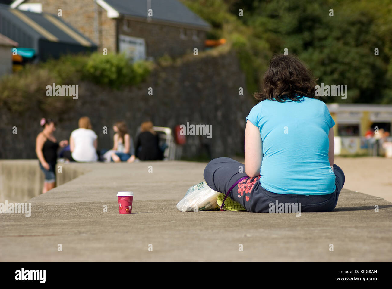 Girl sitting alone on a wall looking at a group of friends in Newquay ...