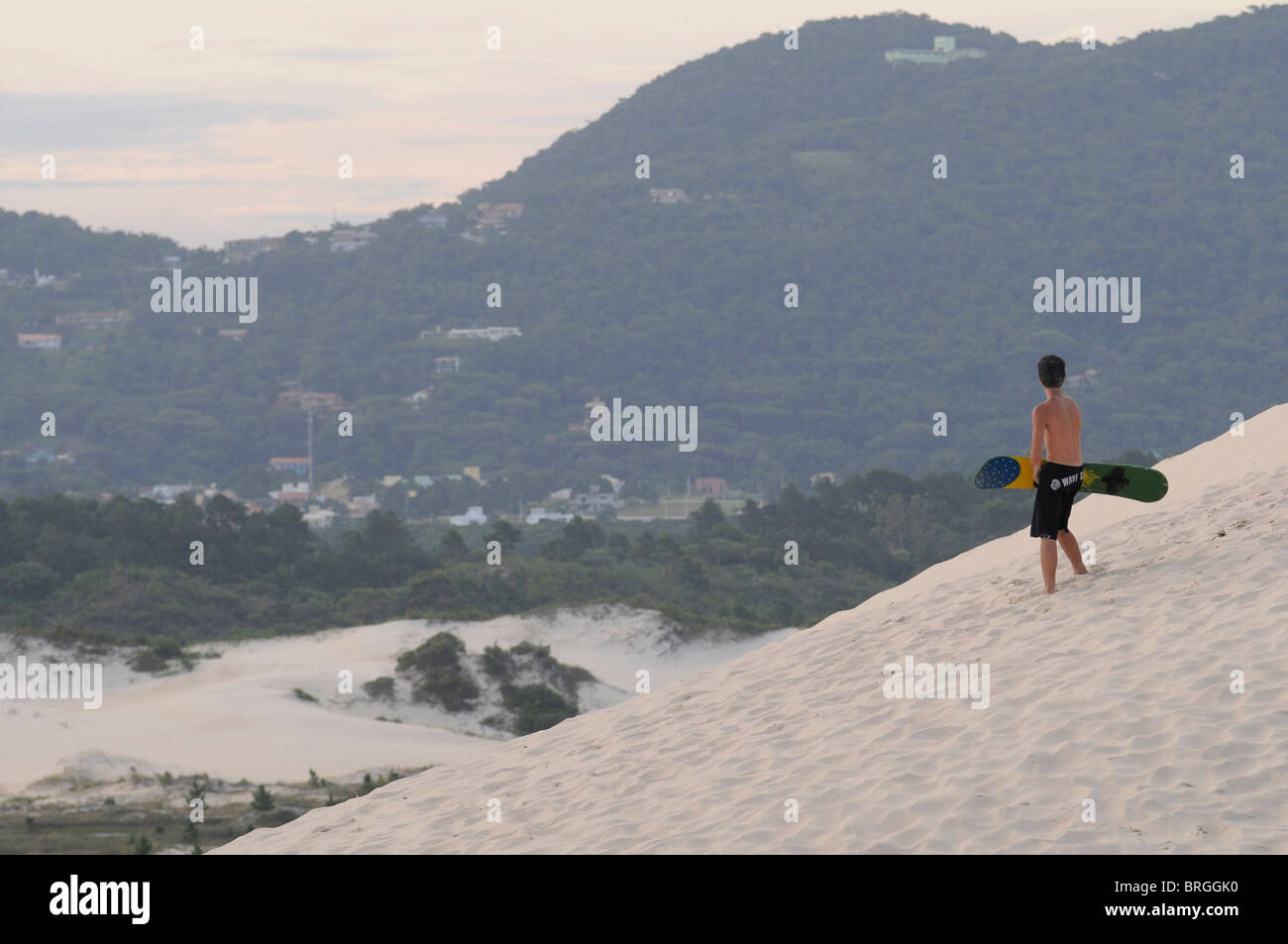 Brazilian teenage sand boarder preparing to surf down a steep sand dune ...