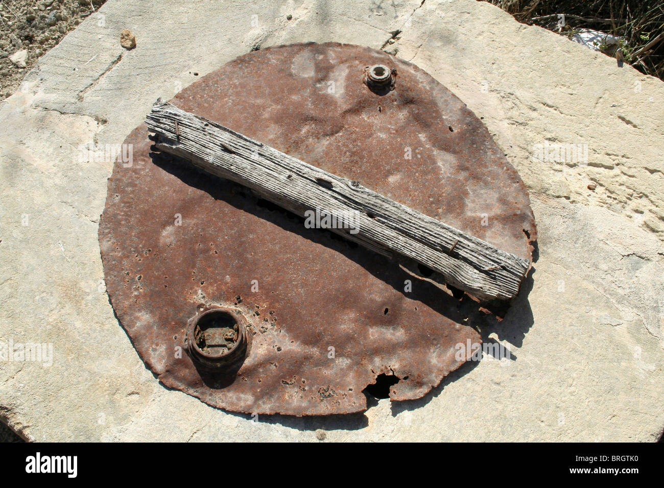 a rusty manhole cover with a piece of bleached wood attached looking ...