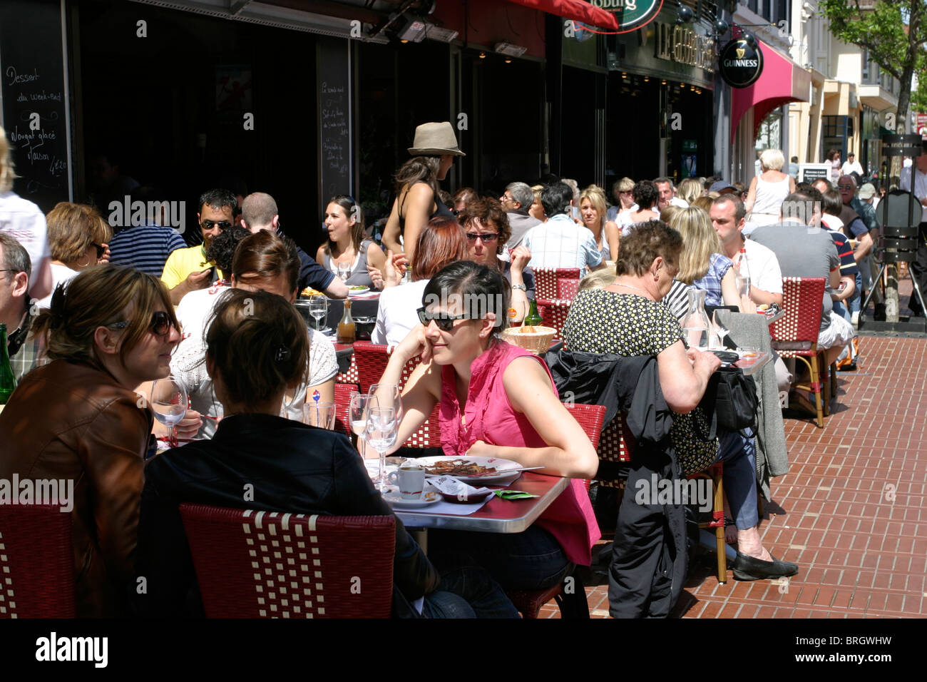 Tourists eating meal at restaurant with outdoor tables on pavement ...
