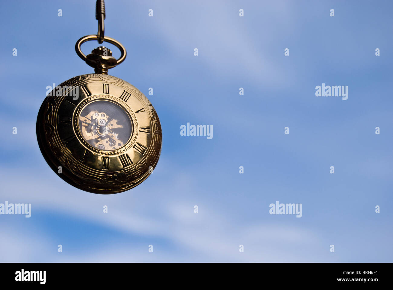 gold skeleton half face pocket watch and chain against blue sky ...