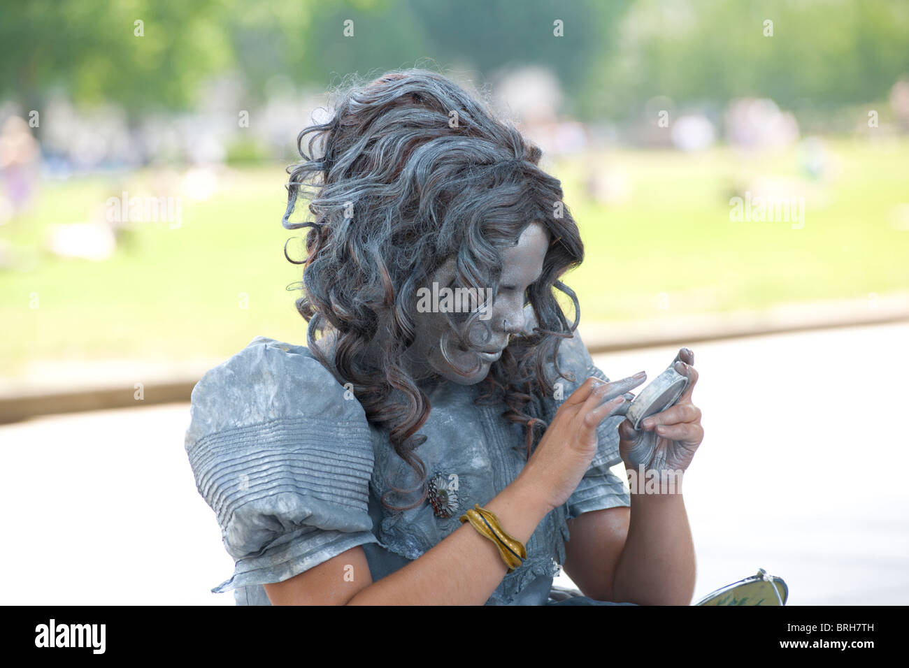 A female street performer applies silver make-up prior to performing on ...