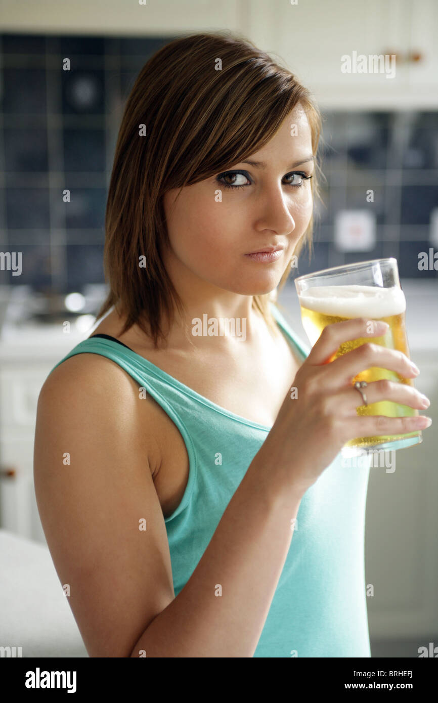 Woman standing in her kitchen holding a pint glass of lager Stock Photo ...