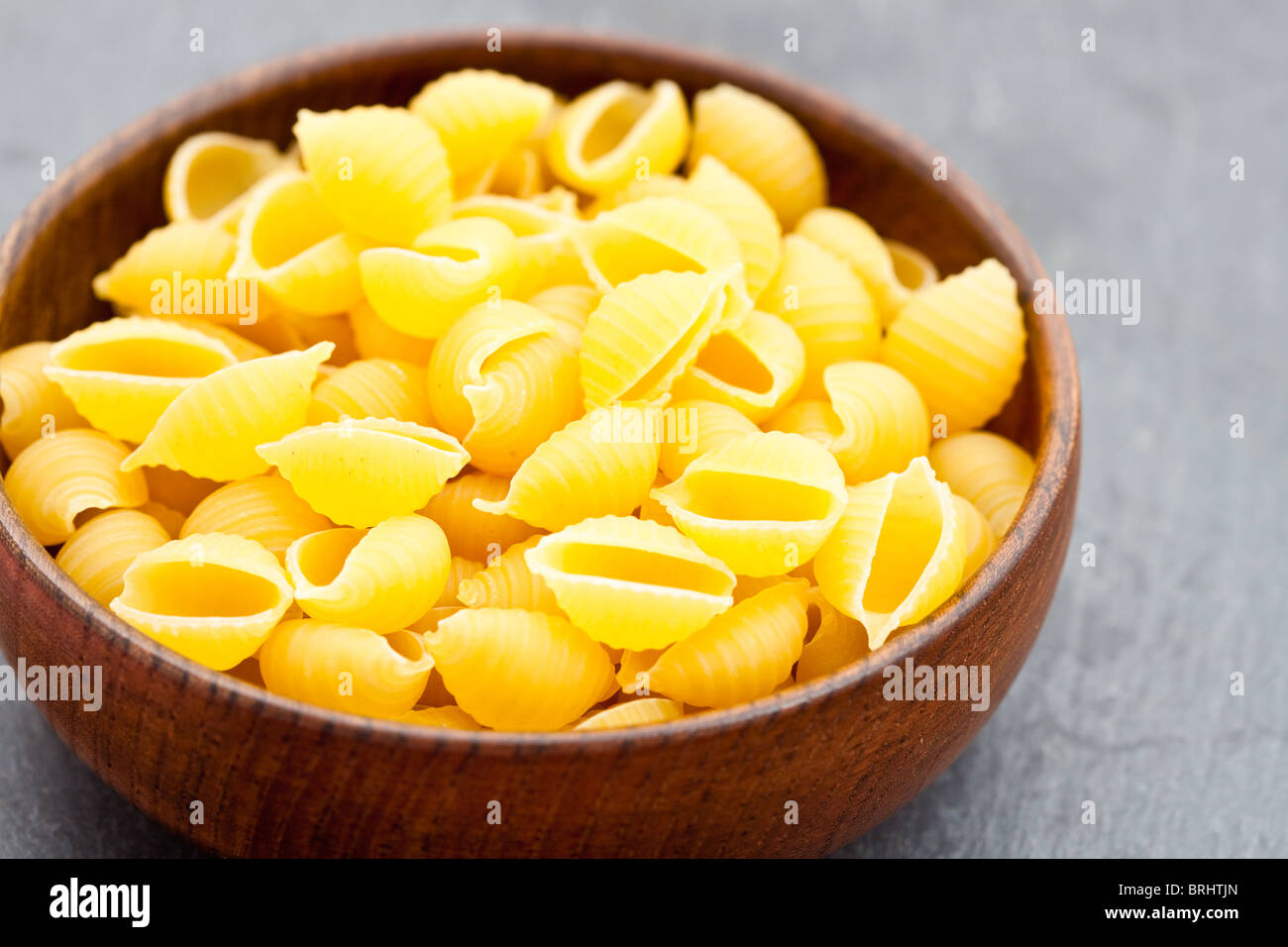 Uncooked Conchiglie pasta shells in a wooden bowl Stock Photo - Alamy