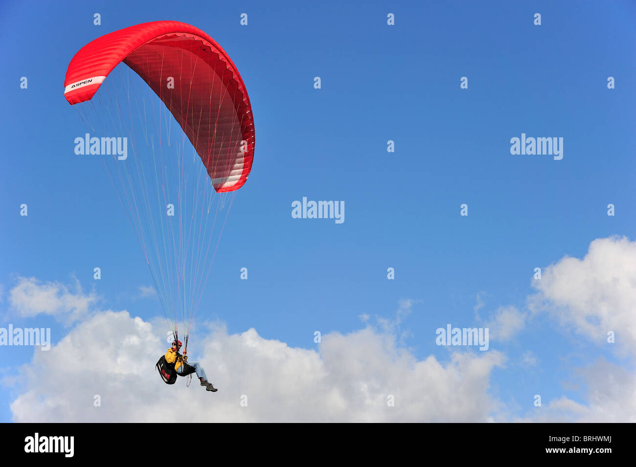 Paraglider in flight with red wing / canopy against blue cloudy sky ...