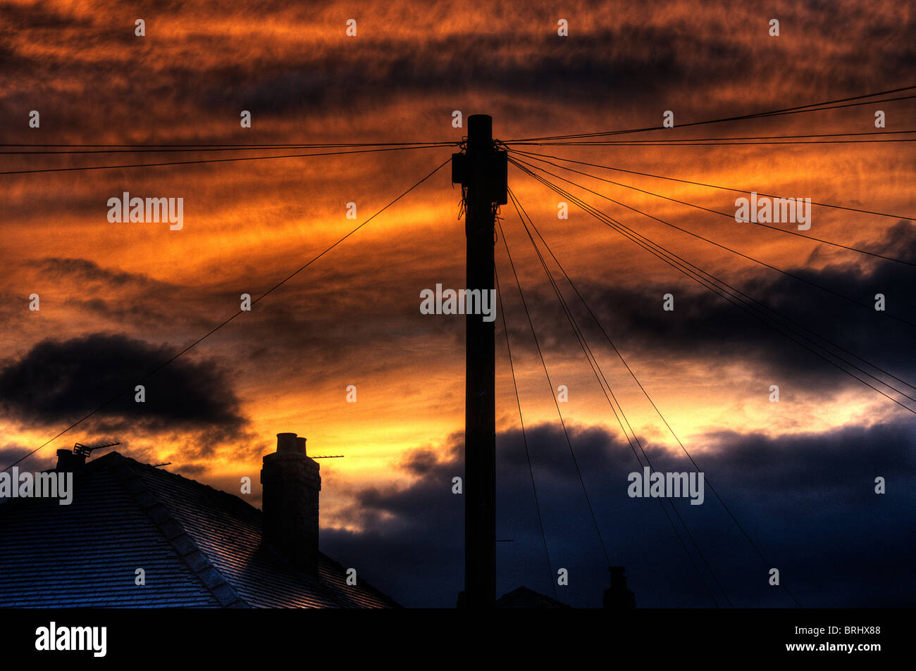 Dramatic sunset sky showing roof top and chimney and telephone post ...