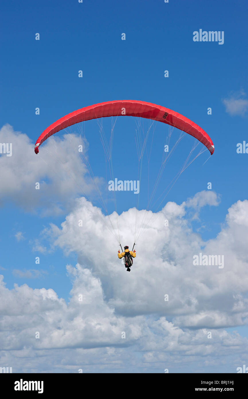 Paraglider in flight with red wing / canopy against blue cloudy sky ...