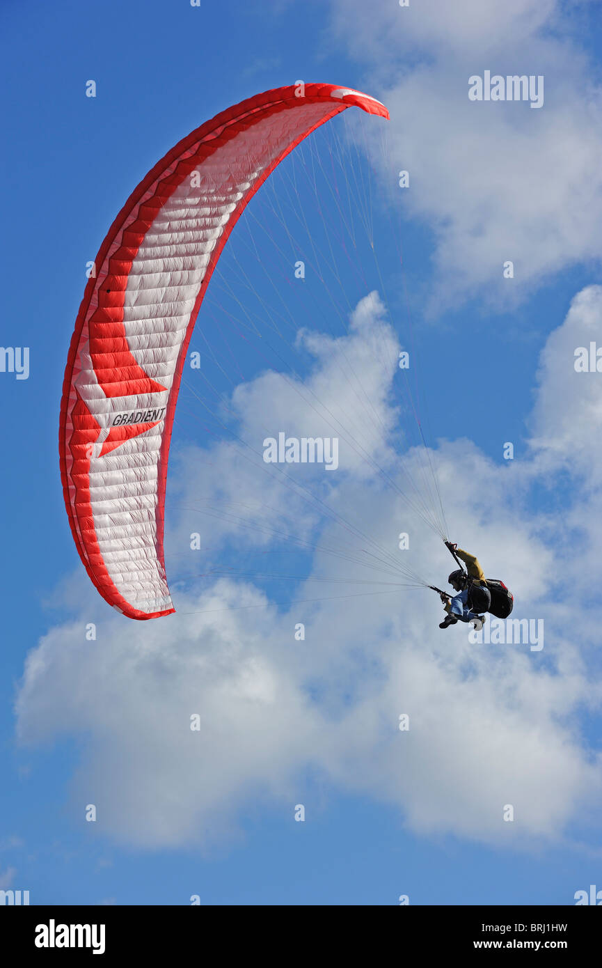 Paraglider in flight with red wing / canopy against blue cloudy sky ...