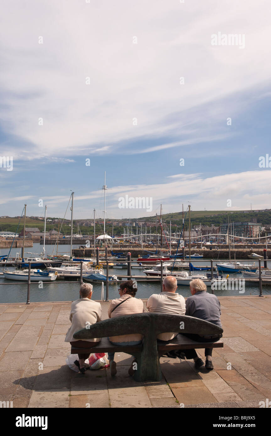 Four people sit on a bench at Whitehaven marina and harbour on the west ...