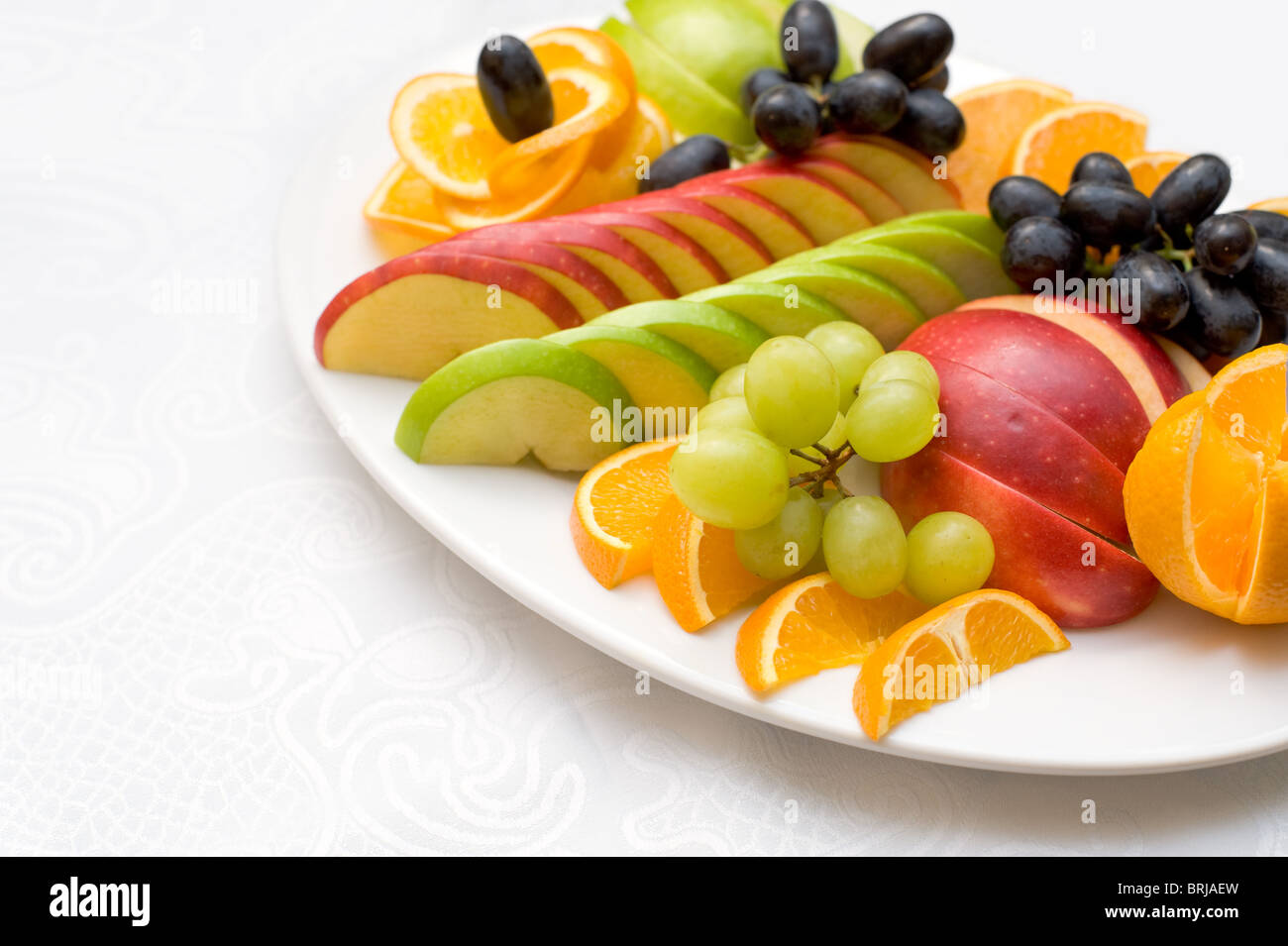 cut apples and oranges with grapes on oval plate, shallow DOF Stock ...