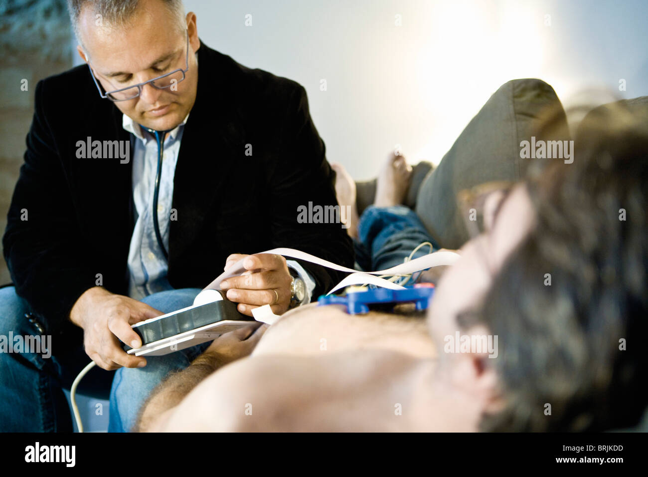 Doctor performing portable EKG (electrocardiogram) on patient in home ...